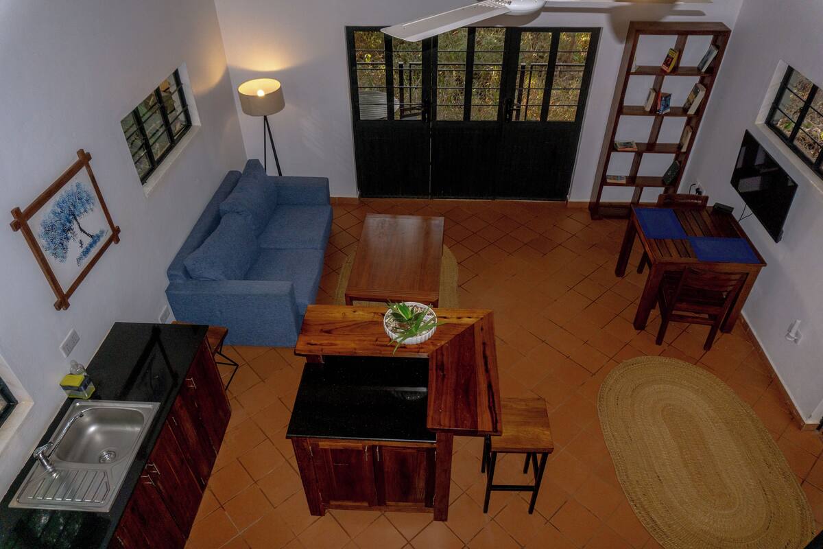Um espaço compacto com cozinha americana, sofá, mesa de jantar com cadeiras, televisão e estante.