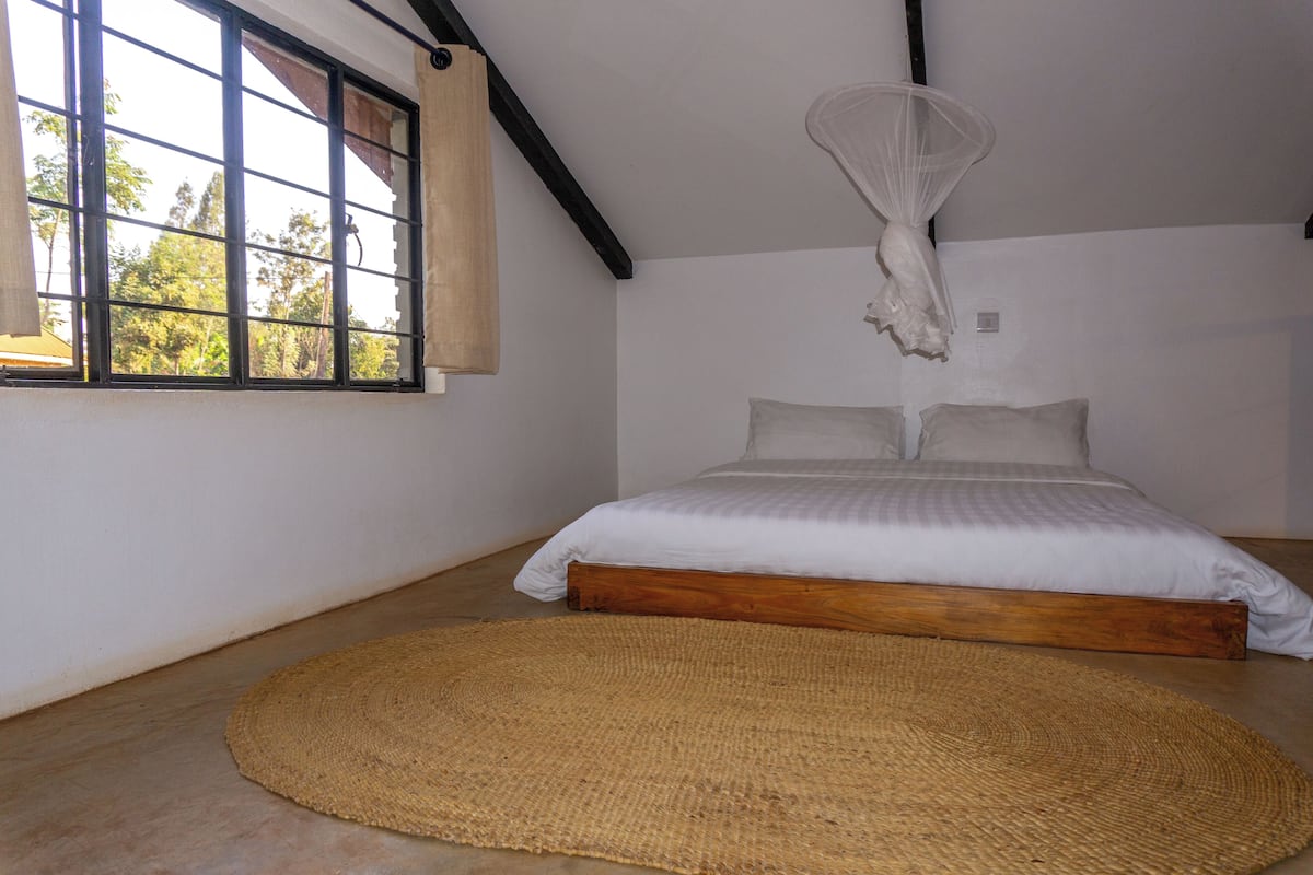 Quarto com uma cama grande, tapete tecido, janela com cortinas e luminária pendente.