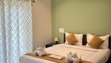Quarto de hotel com cama, mesa de cabeceira, luminária e cortina estampada.