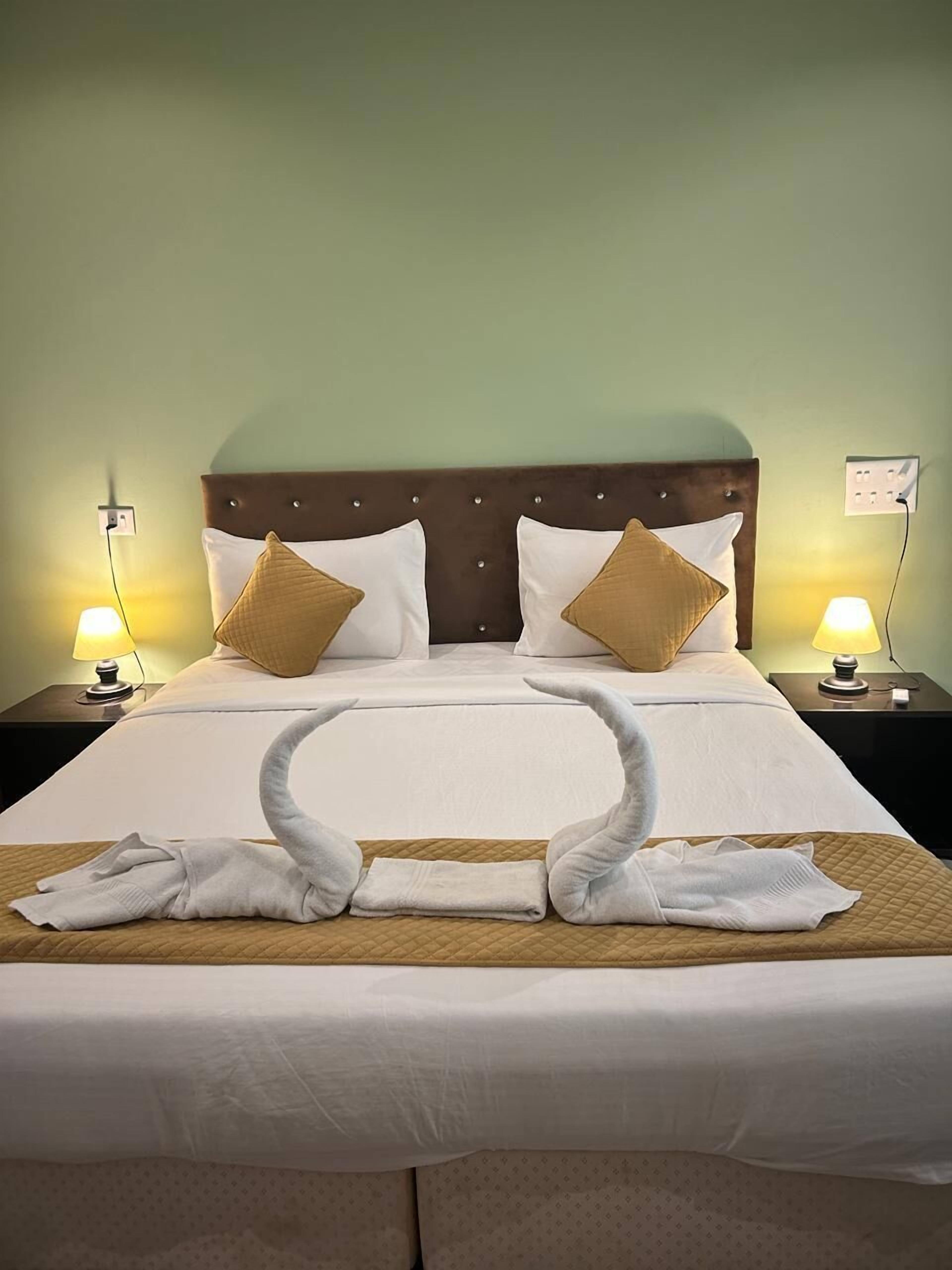 Quarto de hotel com uma cama grande, duas mesas de cabeceira e encosto de cama.
