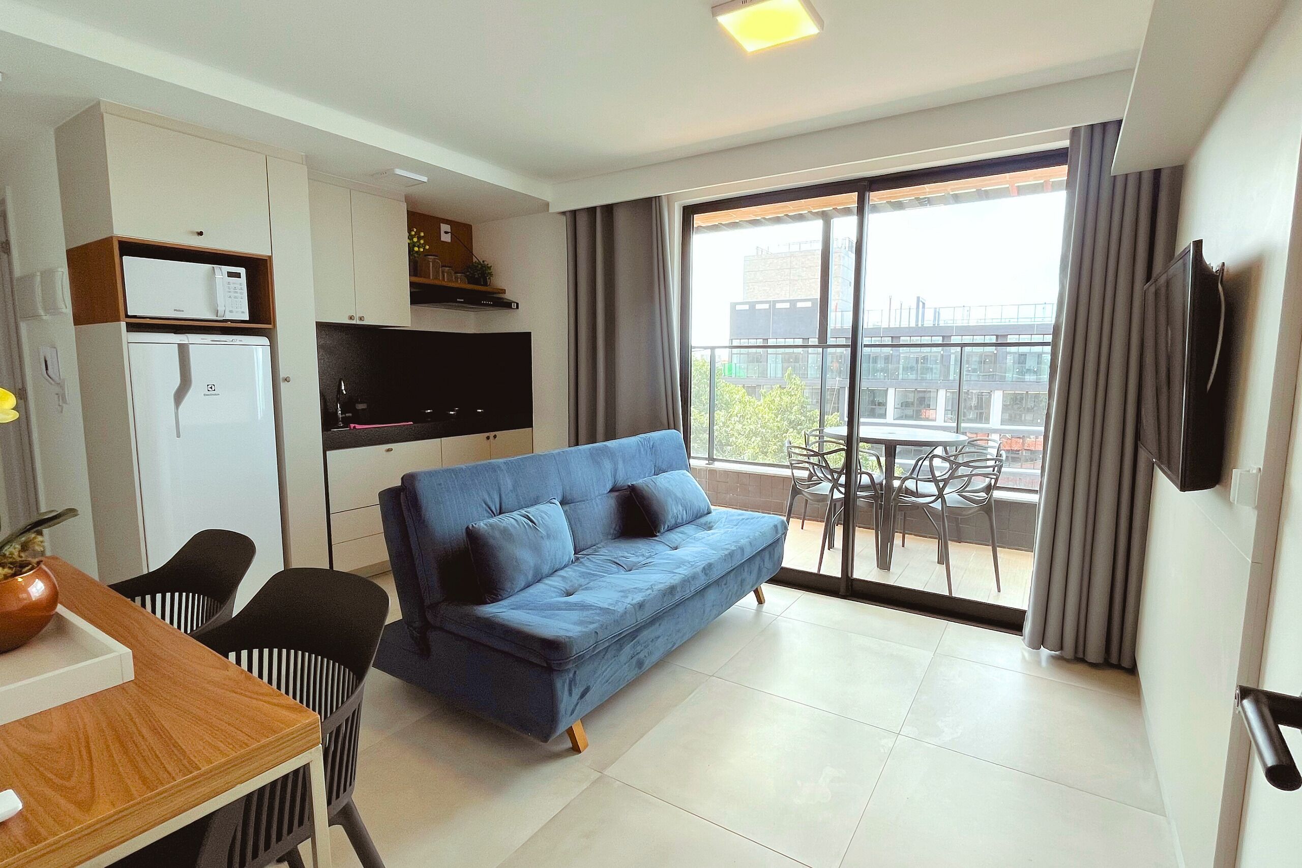 Uma sala de estar moderna com sofá, mesa de jantar, cadeiras, televisão e uma varanda com vista.