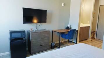 Quarto de hotel com cama, escrivaninha com cadeira, televisão, micro-ondas e mini-geladeira.