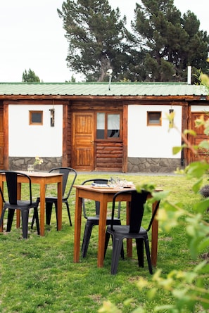 Uma cabana rústica com alicerce de pedra, portas de madeira e telhado de metal verde.