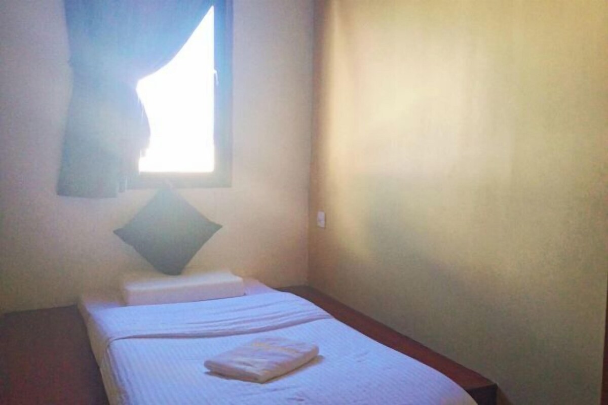 Quarto pequeno e simples com uma cama de solteiro, um travesseiro e uma janela com cortinas.