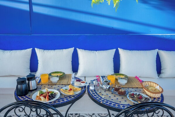 Uma mesa para o café da manhã, duas cadeiras, um sofá com almofadas azuis e uma parede azul.