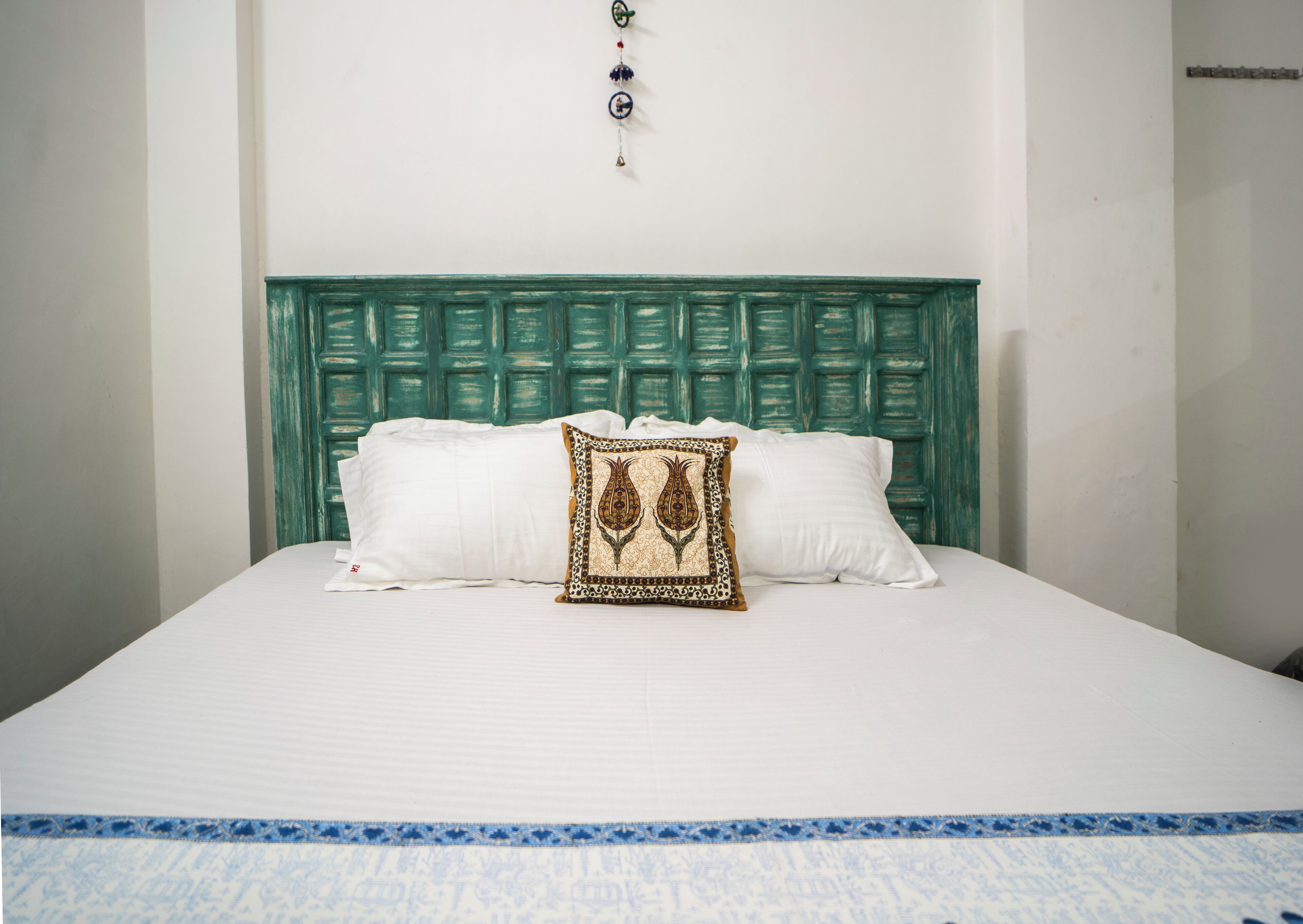 Uma cama com colchão branco, cabeceira verde e travesseiro decorativo.