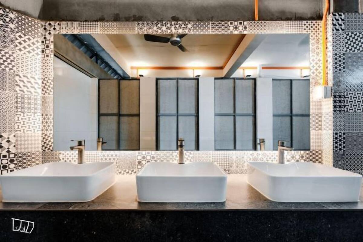 Casa de banho com três lavatórios brancos, um ventilador de teto e azulejos estampados.