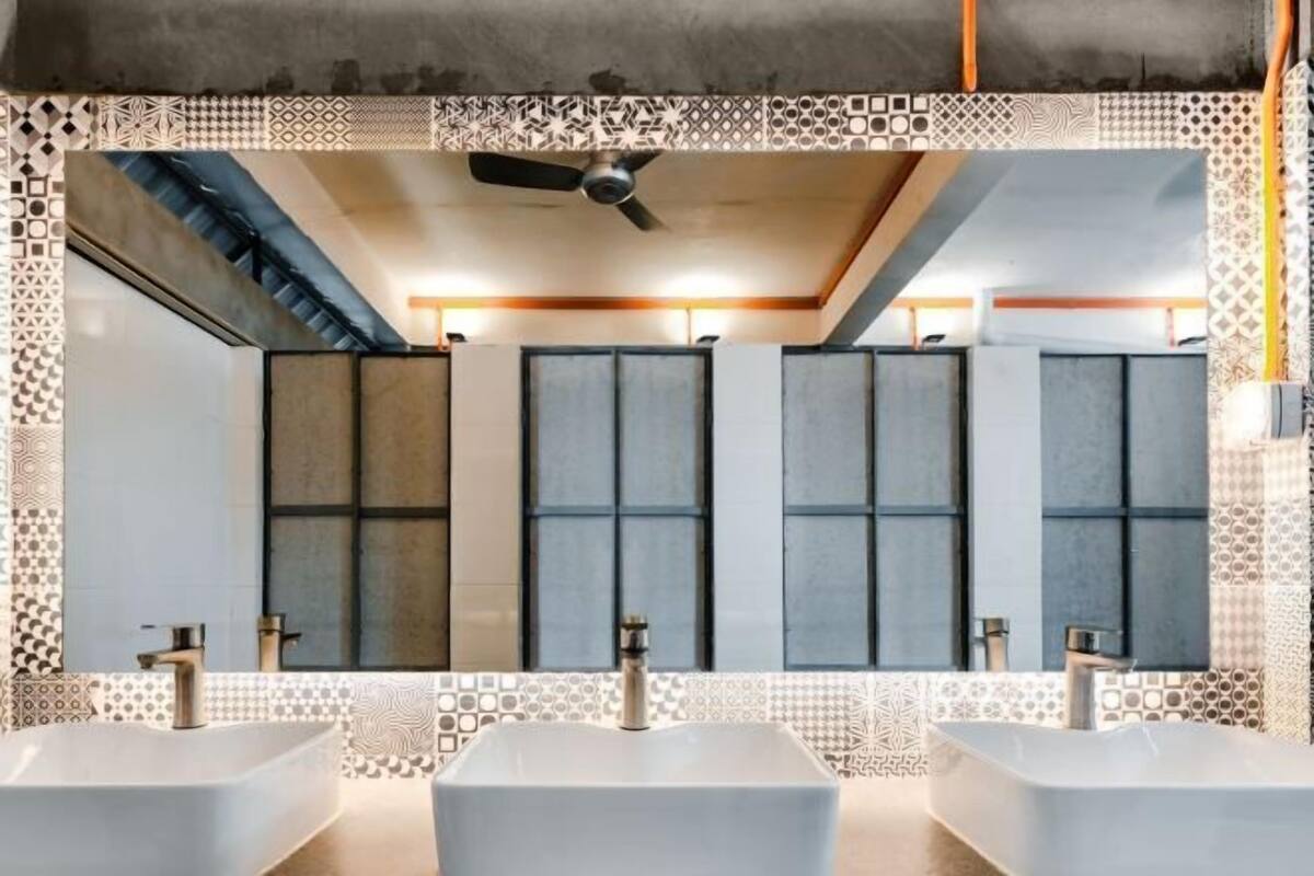 Casa de banho com três lavatórios, ventoinha no teto e azulejos estampados.