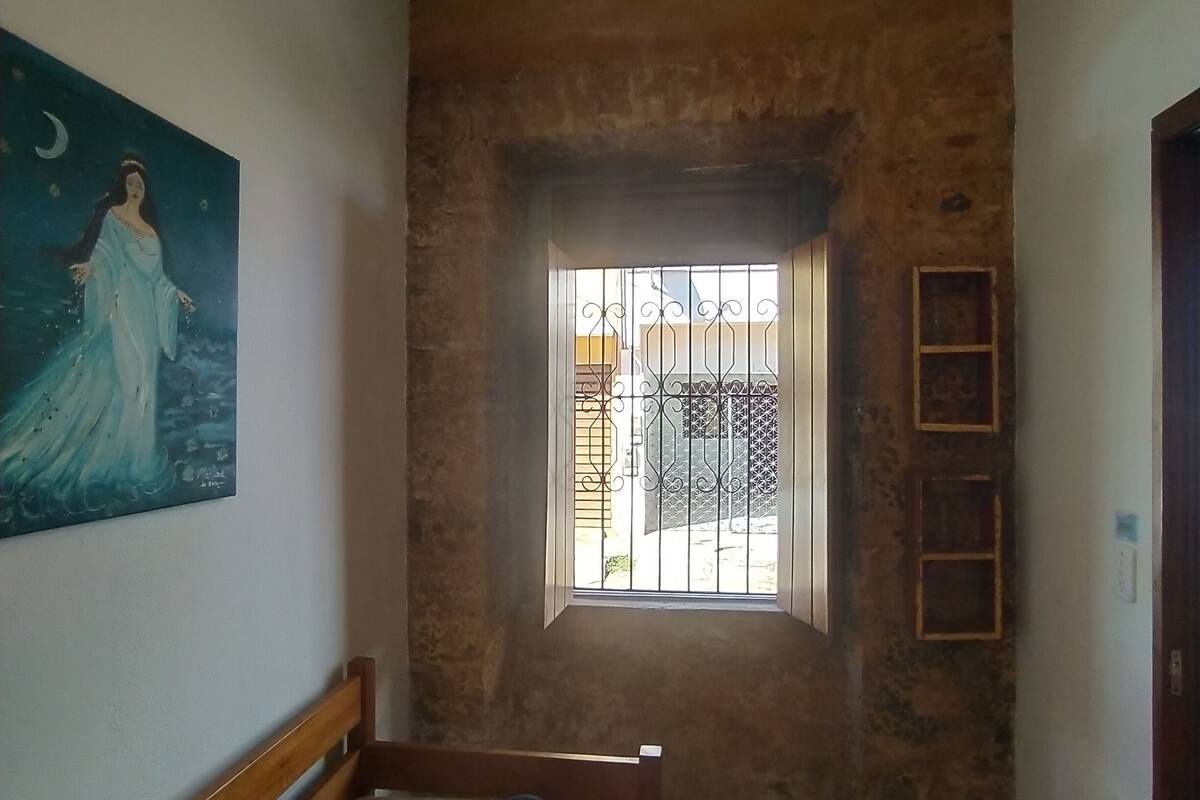 Quarto com cama, ventilador de teto, janela com grades e um quadro na parede.