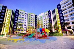 Um parquinho com escorregadores e estruturas de escalada, cercado por edifícios residenciais altos.