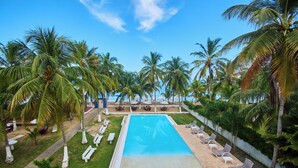 Uma piscina rodeada por palmeiras e espreguiçadeiras, com vista para o oceano.