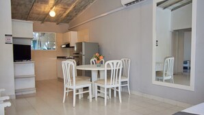 Cozinha compacta com geladeira, fogão e micro-ondas. Há uma mesa de jantar com quatro cadeiras e um vaso com flores. Um espelho grande está na parede.