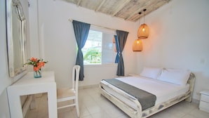 Quarto com cama, mesa de cabeceira, cadeira, janela com cortinas e luminária pendente.