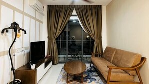 Uma sala de estar com sofá, televisão, ventilador de teto e uma janela grande com cortinas.