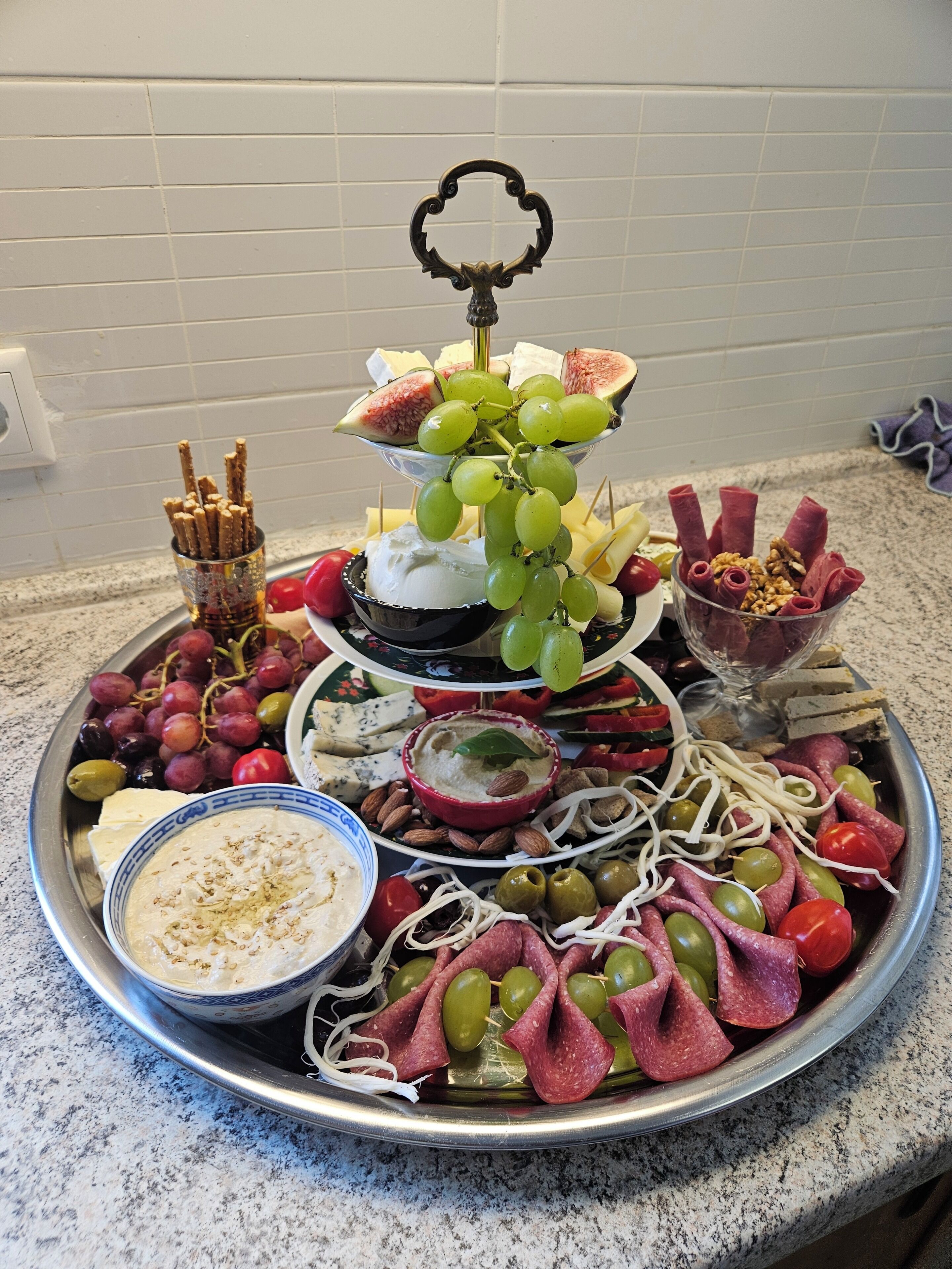 Um prato escalonado com diversos queijos, uvas, azeitonas e carnes.