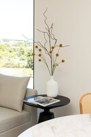 Uma sala de estar moderna com um sofá bege, uma mesa redonda com uma revista e um vaso branco com flores amarelas.