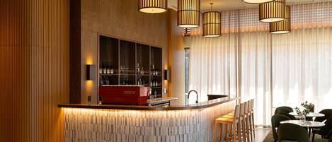 Uma área de bar moderna com balcão curvo, painéis de madeira e luminárias pendentes.