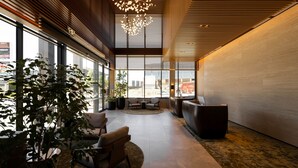 Um lobby moderno com grandes janelas, um lustre central e áreas de estar.