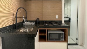 Uma cozinha moderna com bancada preta, eletrodomésticos de aço inoxidável e painéis de madeira na parede.