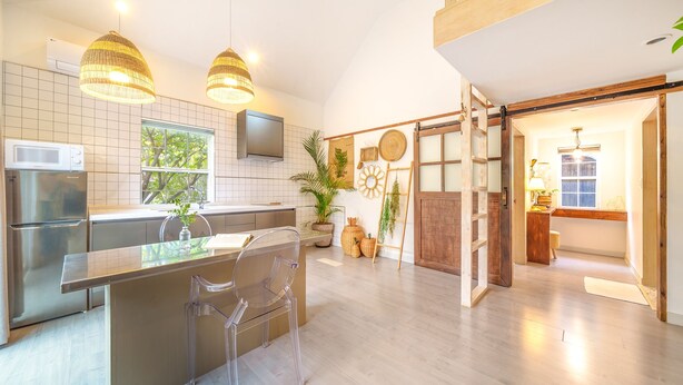 Cozinha moderna com uma ilha grande, eletrodomésticos de aço inoxidável e sala de jantar com cadeiras transparentes.