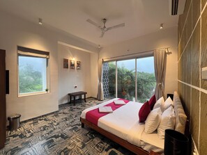 Quarto com uma cama grande, um ventilador de teto, janela com vista e uma mesinha.