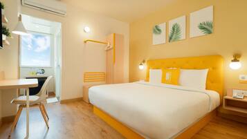 Quarto de hotel com cama, escrivaninha, cadeira, guarda-roupa e janela.