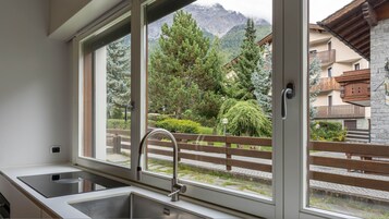 Cozinha com pia de aço inoxidável e janela com vista para uma varanda com guarda-corpo de madeira.