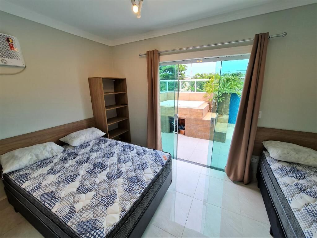 Quarto com duas camas, uma prateleira de madeira e uma porta de vidro deslizante para área externa.