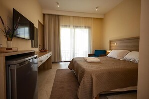 Quarto de hotel com cama, televisão, escrivaninha e janela com cortinas.