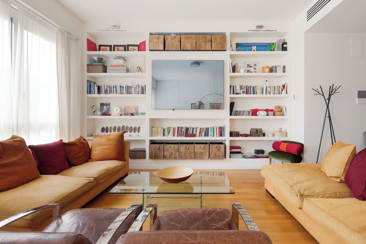 Uma sala de estar moderna com um sofá, poltronas, uma mesa de centro e uma estante repleta de livros e objetos decorativos.