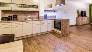 Cozinha moderna com armários brancos, bancada de madeira, forno embutido e área de refeições com mesa e cadeiras.