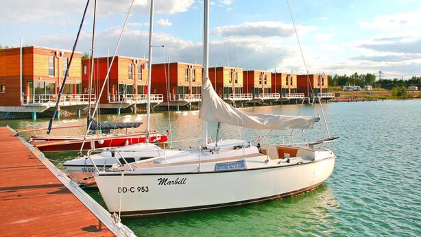 Uma marina com um veleiro branco chamado 'Marbill' atracado num cais de madeira.