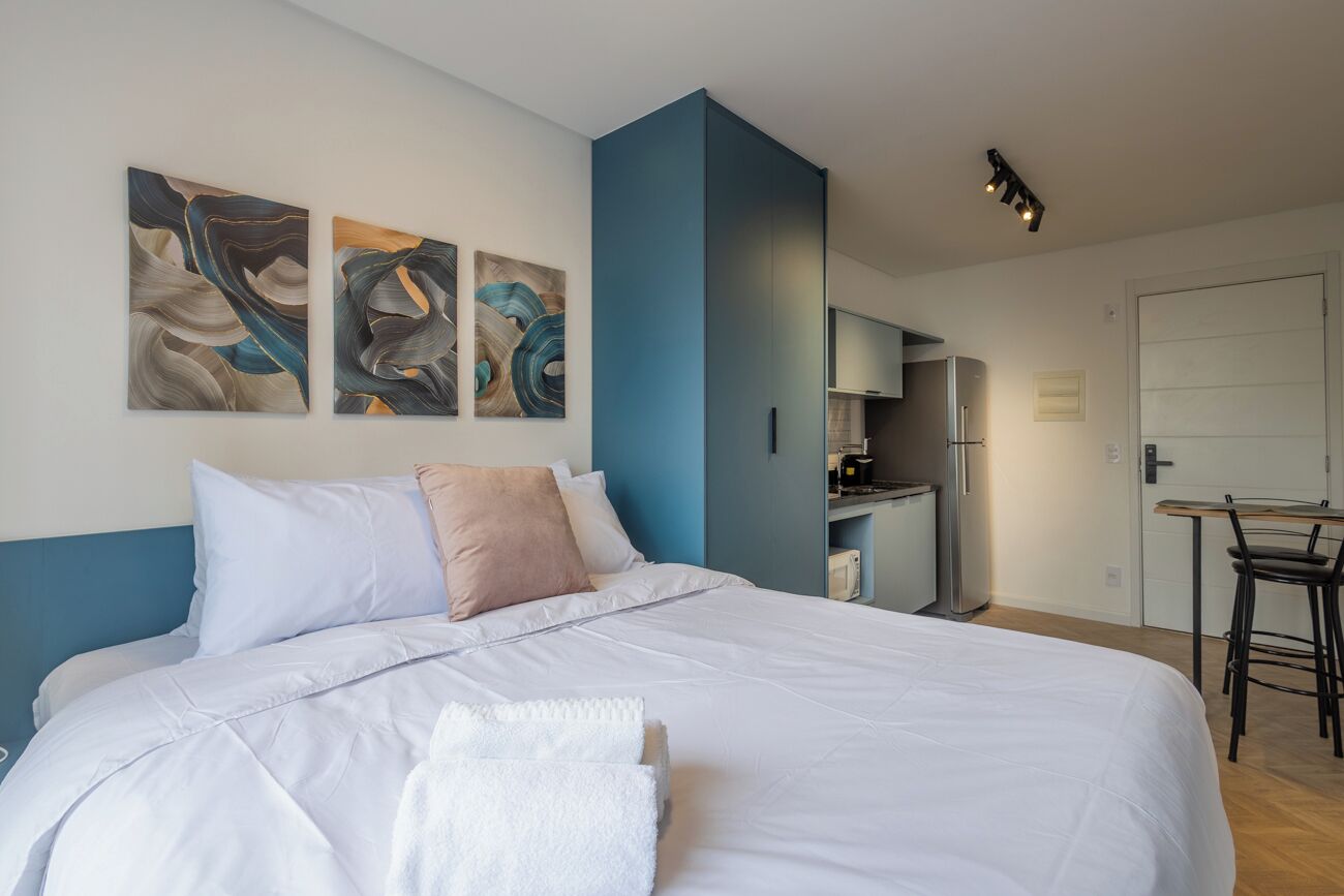 Quarto de hotel moderno com uma cama grande, uma kitchenette e arte abstrata nas paredes.