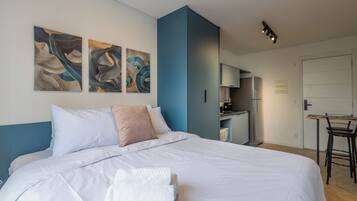 Quarto de hotel moderno com uma cama grande, uma kitchenette e arte abstrata nas paredes.