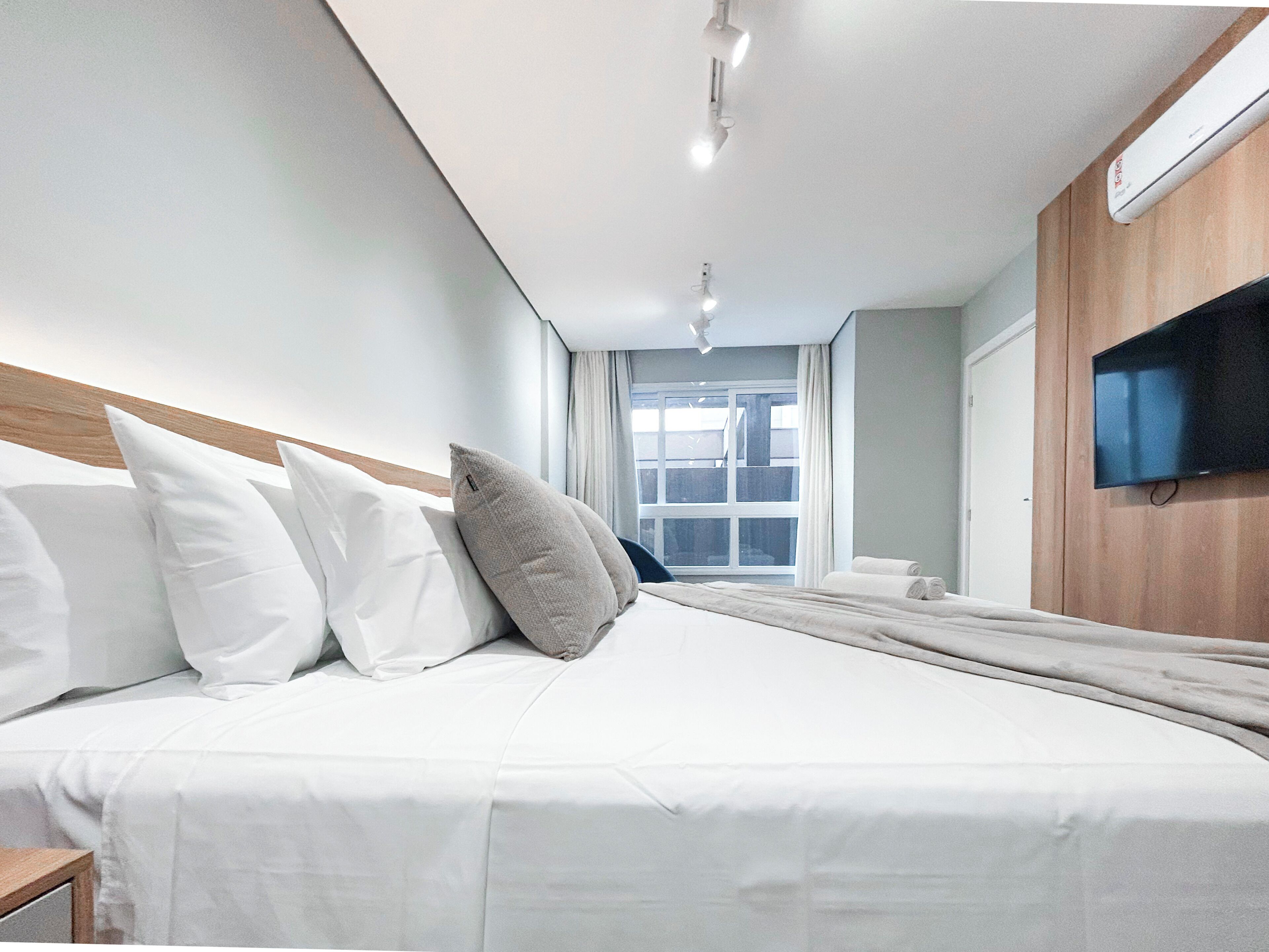 Quarto de hotel com cama, almofadas, televisão e janela.