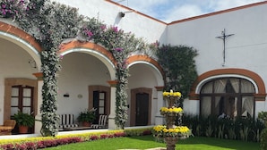 Pátio com fonte, gramado verde e edifício branco com arcos.