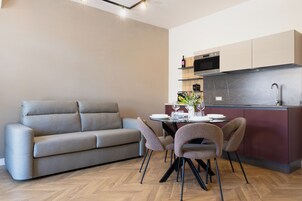 Uma sala de estar moderna com sofá e mesa de jantar, uma cozinha com forno embutido e micro-ondas, e uma pequena ilha com pia.