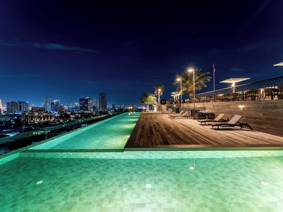 Piscina infinita no terraço com espreguiçadeiras e vista para a cidade à noite.