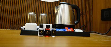 Uma mesa de madeira com um tabuleiro preto contendo uma cafeteira, um copo e três frascos de produtos de higiene pessoal.