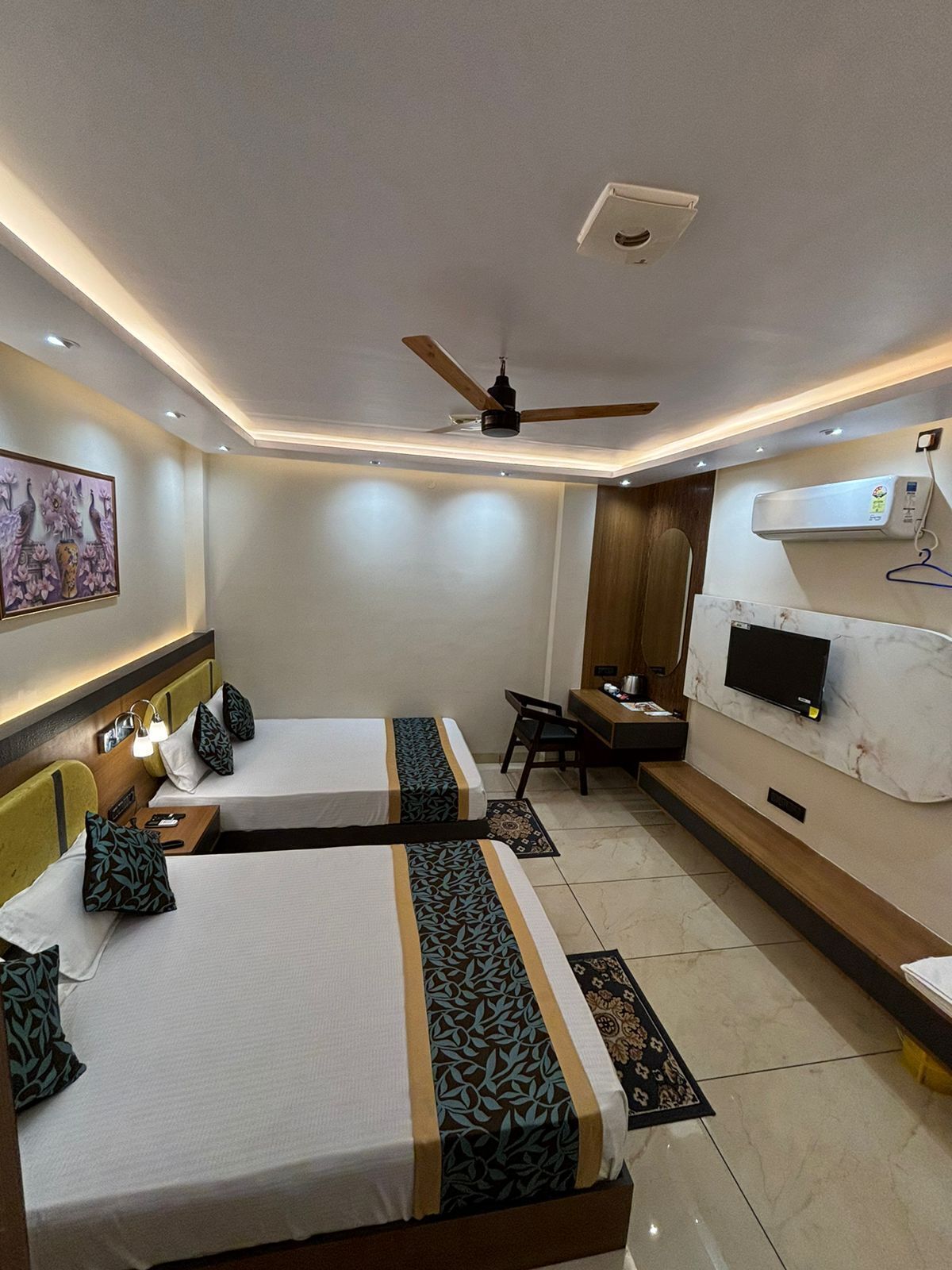 Quarto de hotel com duas camas, uma escrivaninha, televisão e ventoinha no teto.