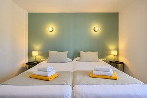 Quarto duplo com duas camas, cada uma com travesseiro, mesa de cabeceira e abajur.