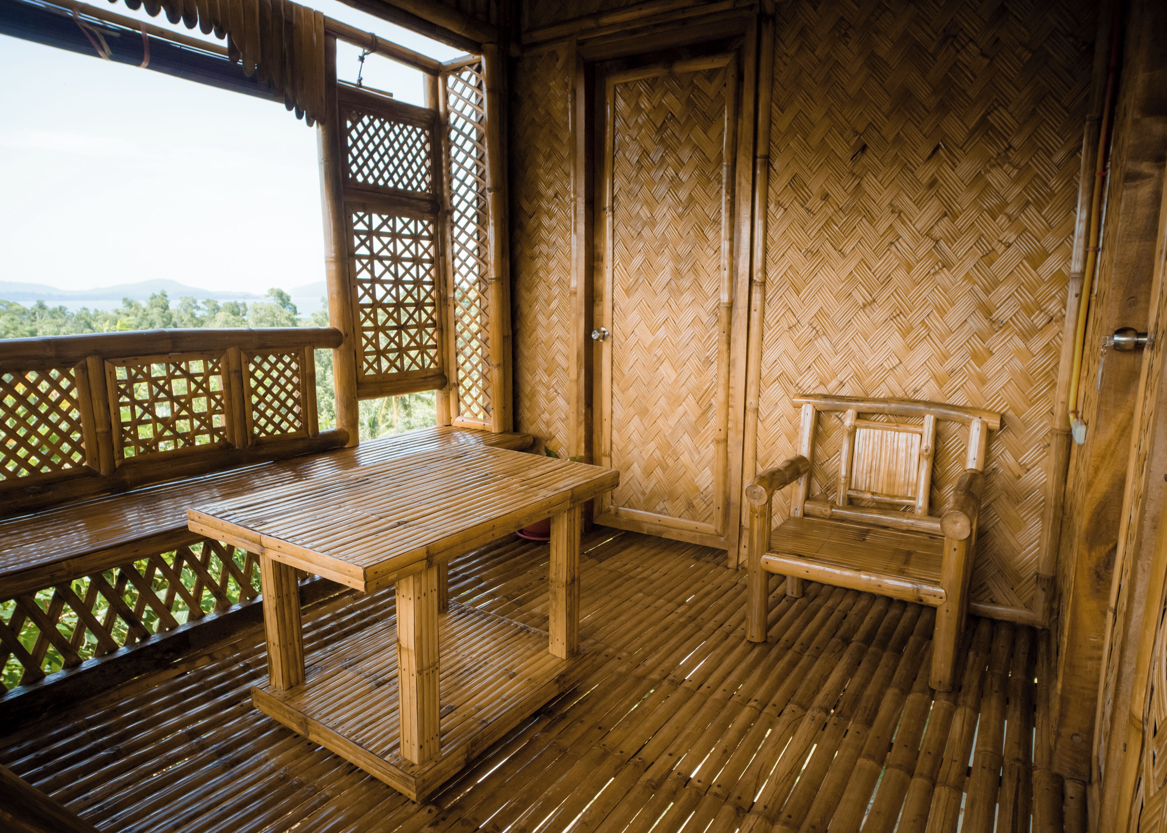 Um deck de madeira com uma mesa e uma cadeira, uma porta de madeira e vista para o exterior.