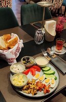Uma mesa de jantar com diversos alimentos, incluindo pão, azeitonas, queijo, ovos e legumes.