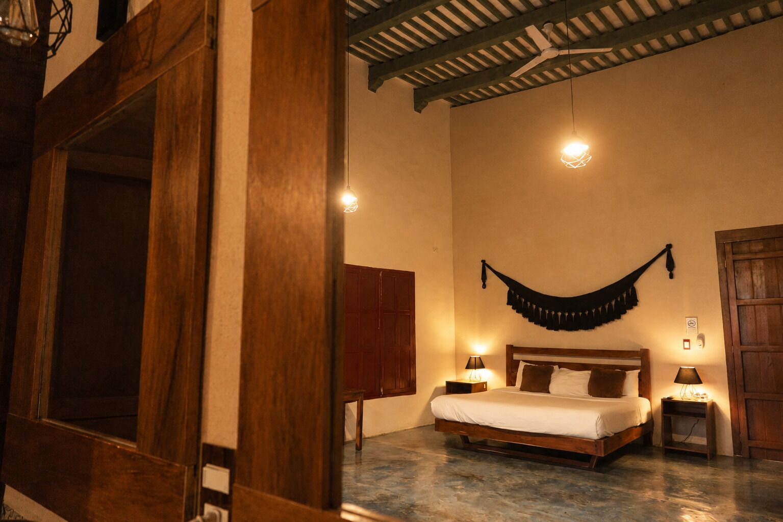 Quarto com cama de madeira, duas luminárias de cabeceira, uma rede e um ventilador de teto.