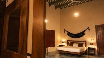 Quarto com cama de madeira, duas luminárias de cabeceira, uma rede e um ventilador de teto.