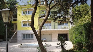 Um pátio com piscina, um edifício amarelo e uma escadaria que leva a um andar superior.