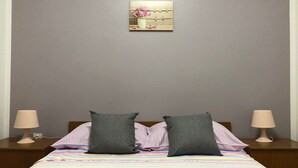 Quarto com cama, duas almofadas, mesa de cabeceira com abajur e quadro na parede.