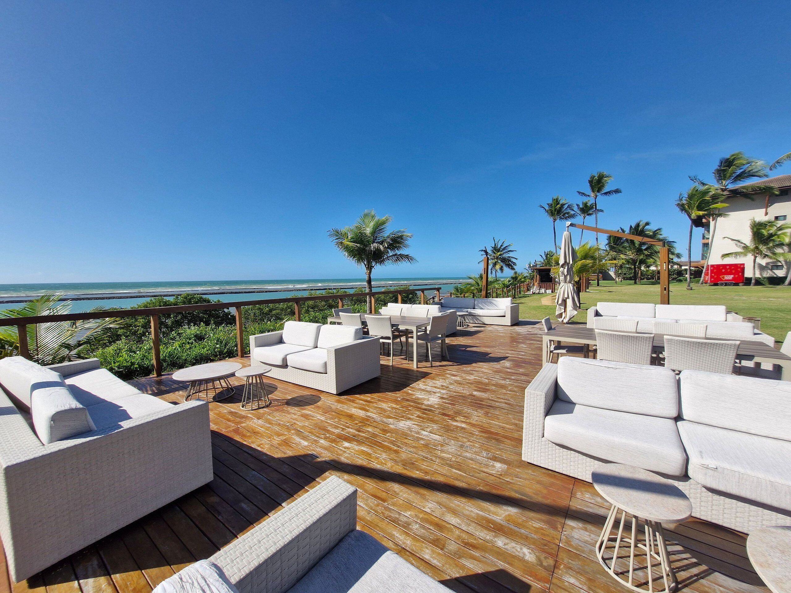 Um terraço com área de estar ao ar livre, vista para o oceano e palmeiras.