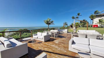 Um terraço com área de estar ao ar livre, vista para o oceano e palmeiras.