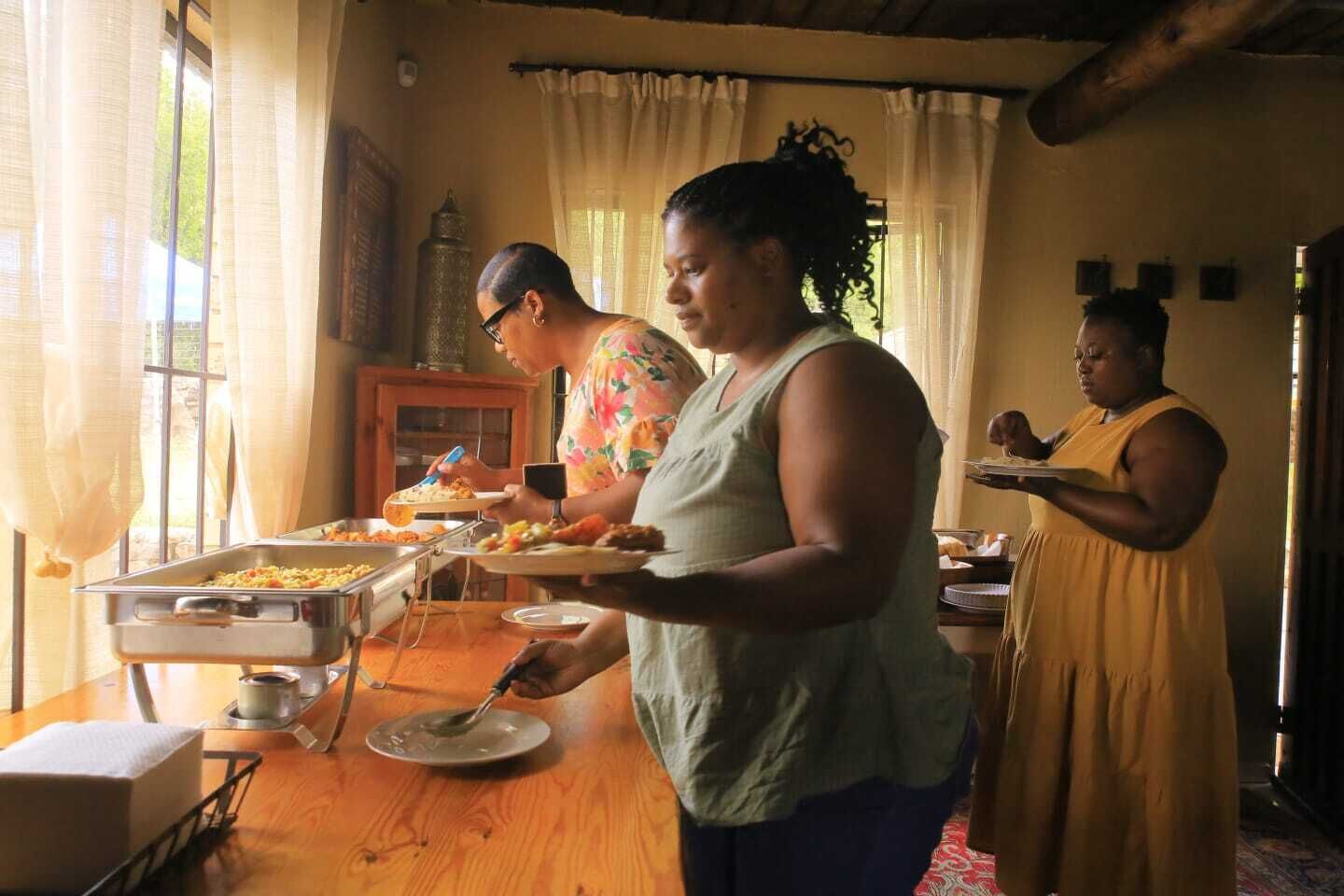 Um quarto com uma mesa de madeira, um buffet montado e uma pessoa servindo comida.
